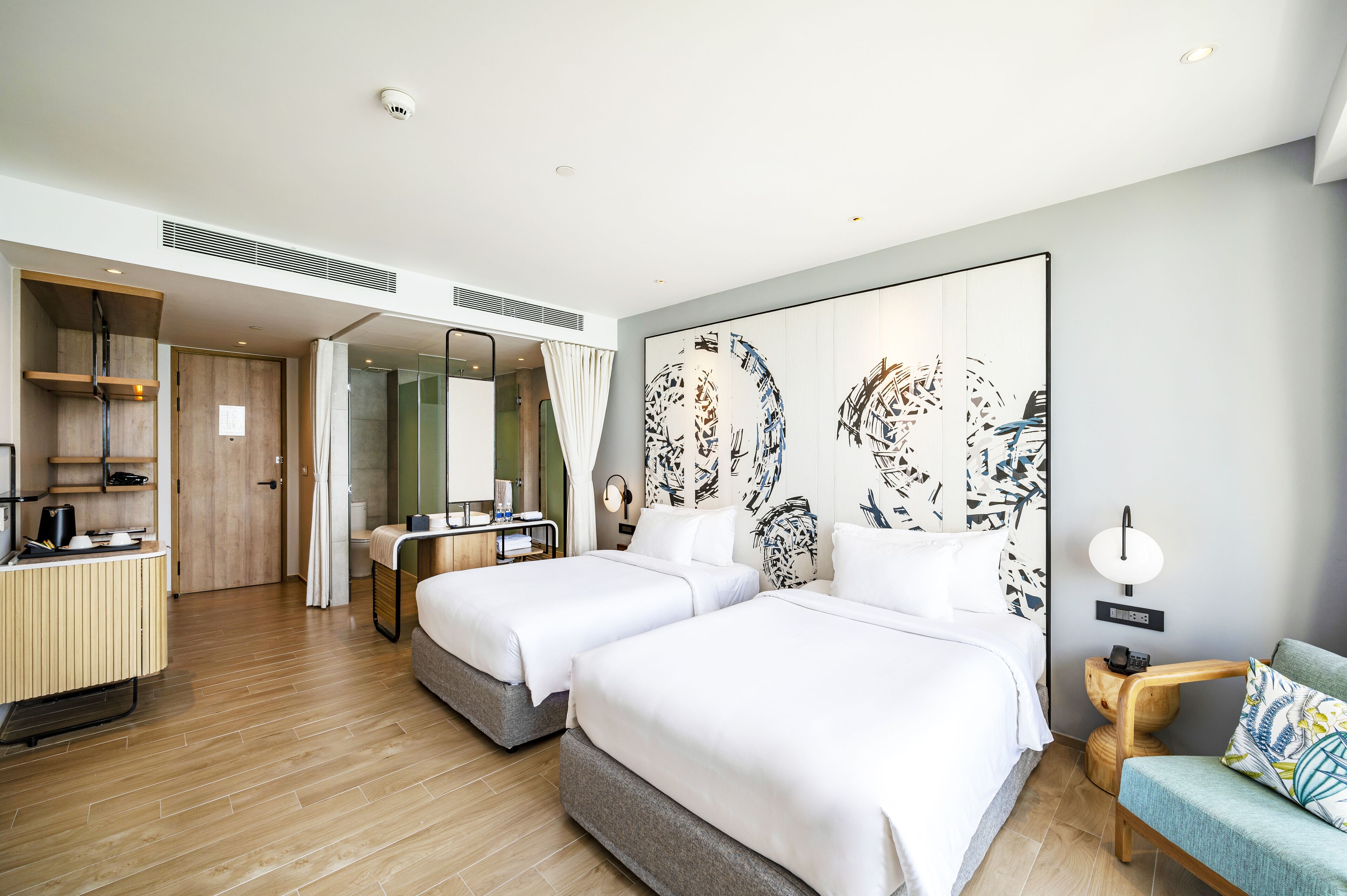 Quarto de hotel moderno com duas camas, uma escrivaninha, toucador e uma grande obra de arte abstrata na parede.