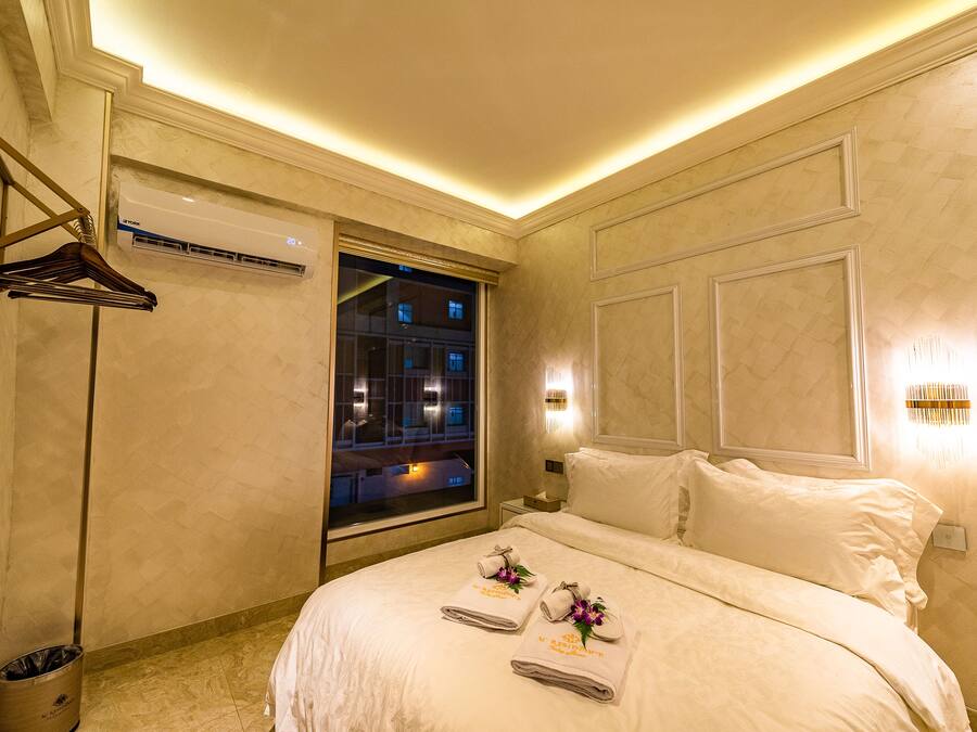 Quarto de hotel com cama bem arrumada, cabideiro, aparelho de ar condicionado, mesa de cabeceira e janela com vista para o exterior.