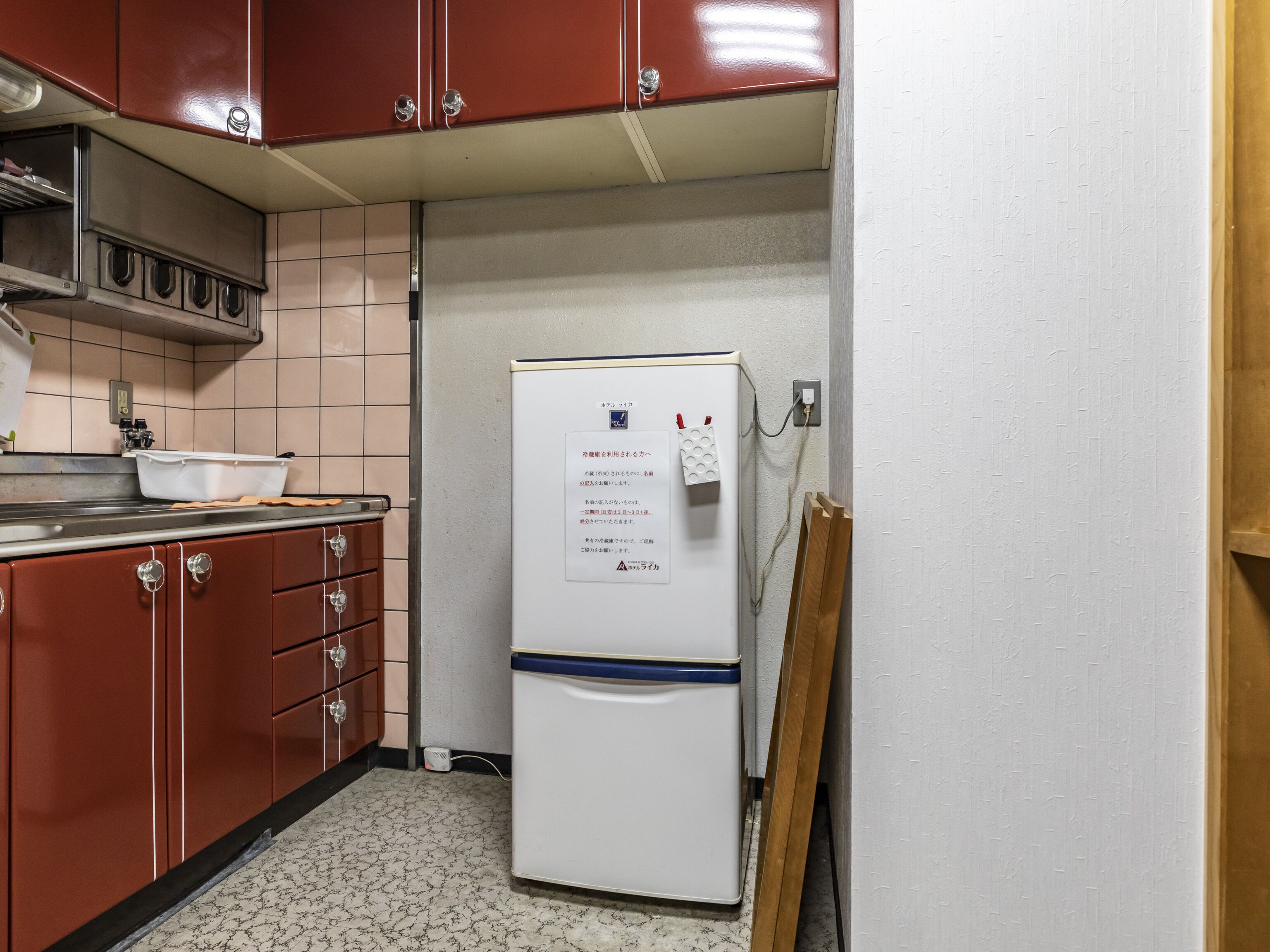 Uma cozinha compacta com armários vermelhos, uma geladeira branca e painel de azulejos.