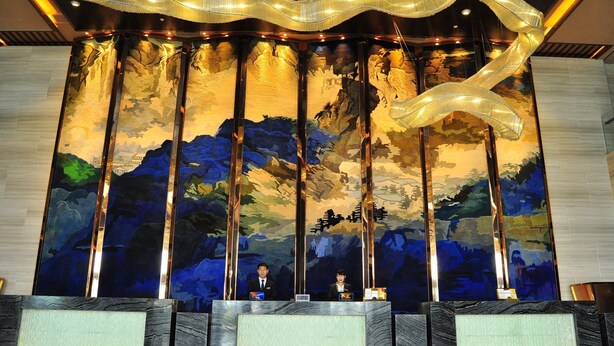 Uma área de recepção com um grande mural de paisagem montanhosa, um lustre moderno e um balcão de atendimento com placa de identificação.