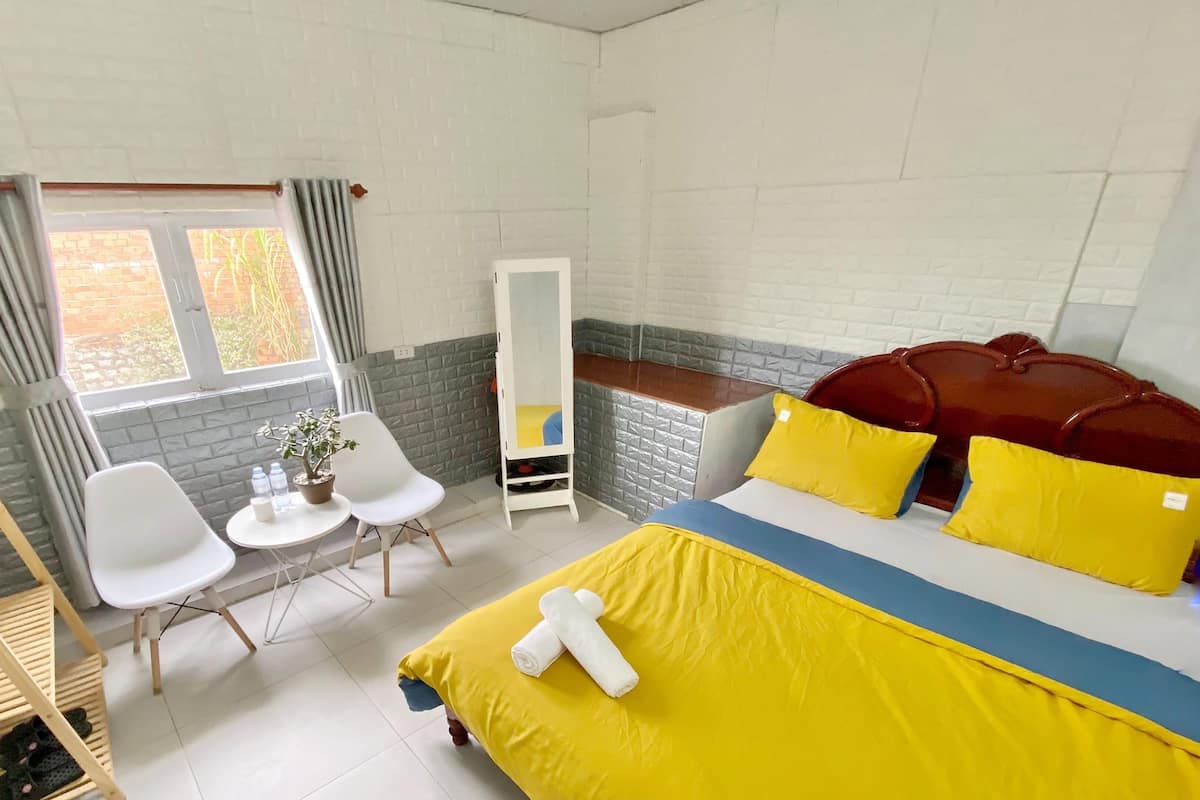 Um quarto com cama, cadeira, mesa pequena e janela.