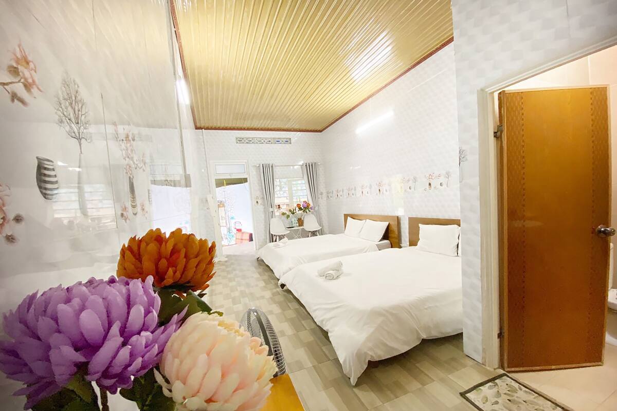 Quarto de hotel com duas camas, teto de madeira, banheiro com chuveiro e uma janela grande.