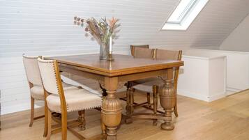 Mesa de jantar com quatro cadeiras, um vaso com flores e teto inclinado com claraboia.