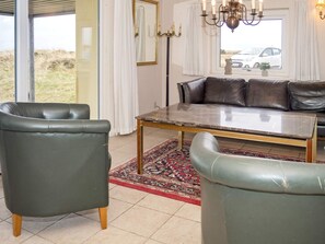 Sala de estar com sofá de couro, duas poltronas, mesa de centro de vidro, tapete estampado e uma grande janela com vista para um carro.