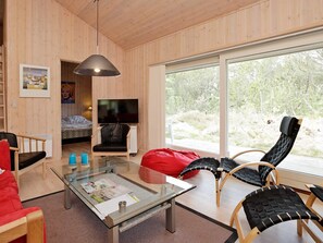 Uma sala de estar moderna com uma mesa de centro de vidro, um pufe vermelho e uma televisão num canto.