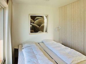 Quarto com duas camas, guarda-roupa de madeira, um quadro emoldurado na parede e janela com cortinas.