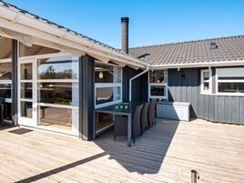 Uma área externa coberta com um deck de madeira, uma mesa com cadeiras e uma chaminé.