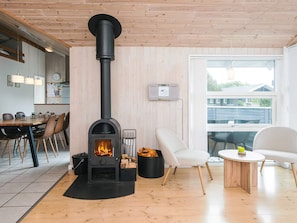 Uma sala de estar moderna com lareira a lenha, espaço para refeições e uma janela ampla.