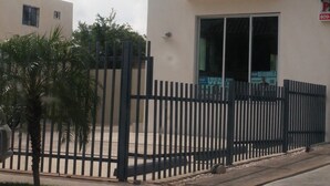 Um edifício com vários andares, varandas, entrada com portão e uma placa visível.