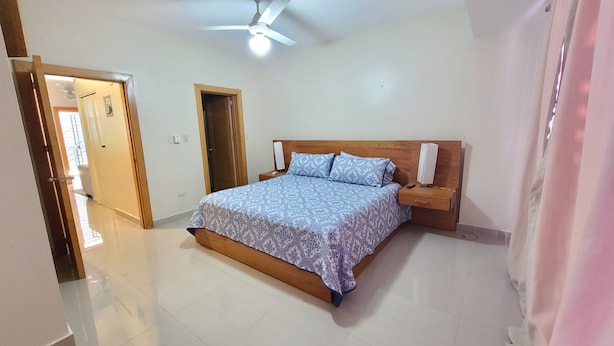 Quarto com cama, cabeceira de madeira, mesas de cabeceira e ventilador de teto.
