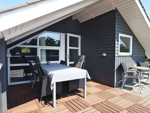 Varanda coberta com mesa e cadeiras, janelas amplas e vista para o exterior.