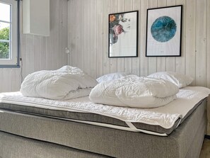 Cama com roupa de cama branca e colchão cinza em quarto com paredes de madeira.