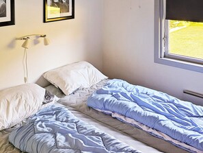 Uma cama de solteiro com edredom azul e branco, luminária de cabeceira e janela com vista para o exterior.