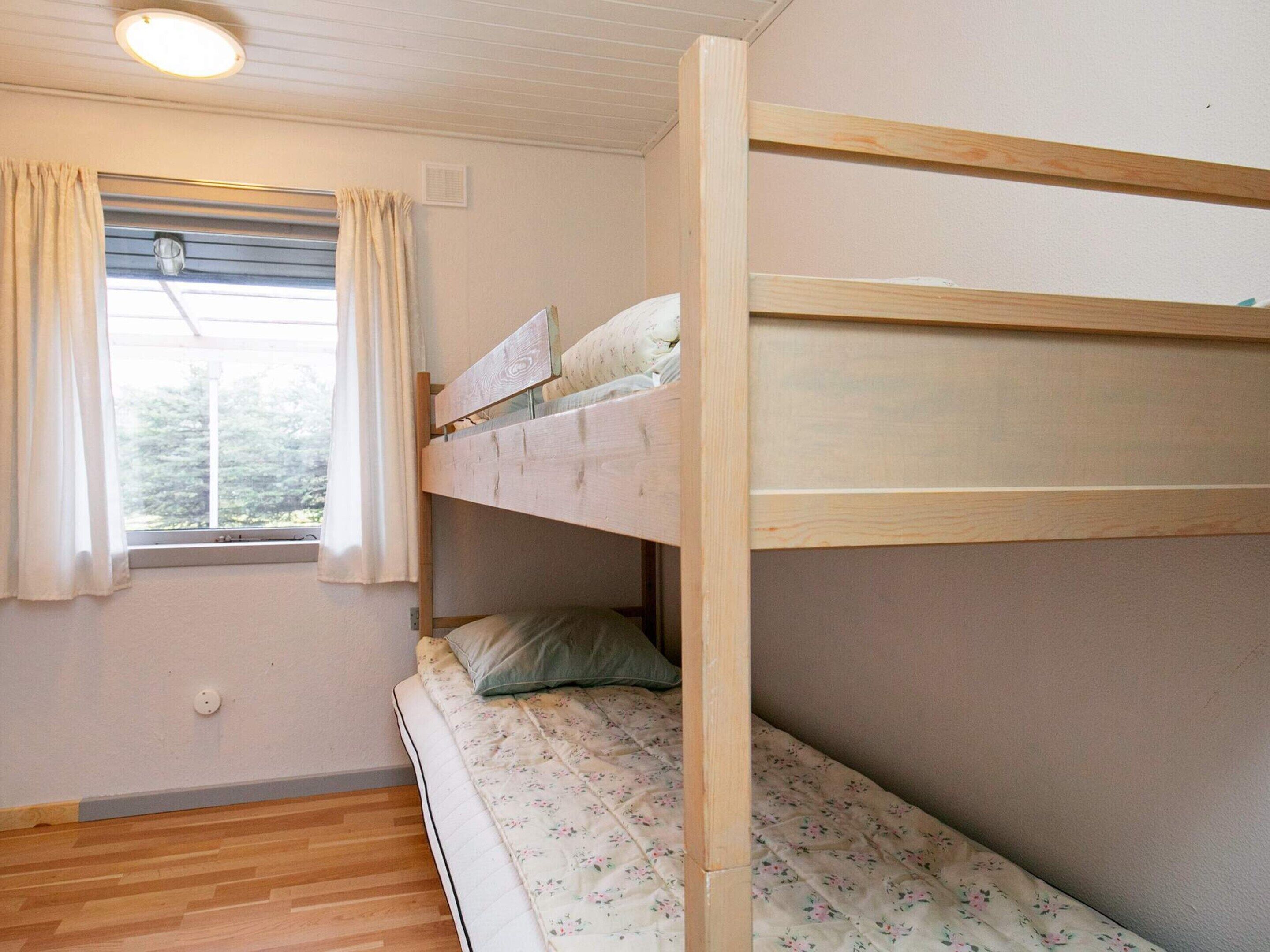 Quarto com beliche, janela, cortinas e piso de madeira.