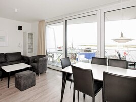 Quarto moderno com mesa de jantar, cadeiras, sofá e uma grande janela com vista para o mar.