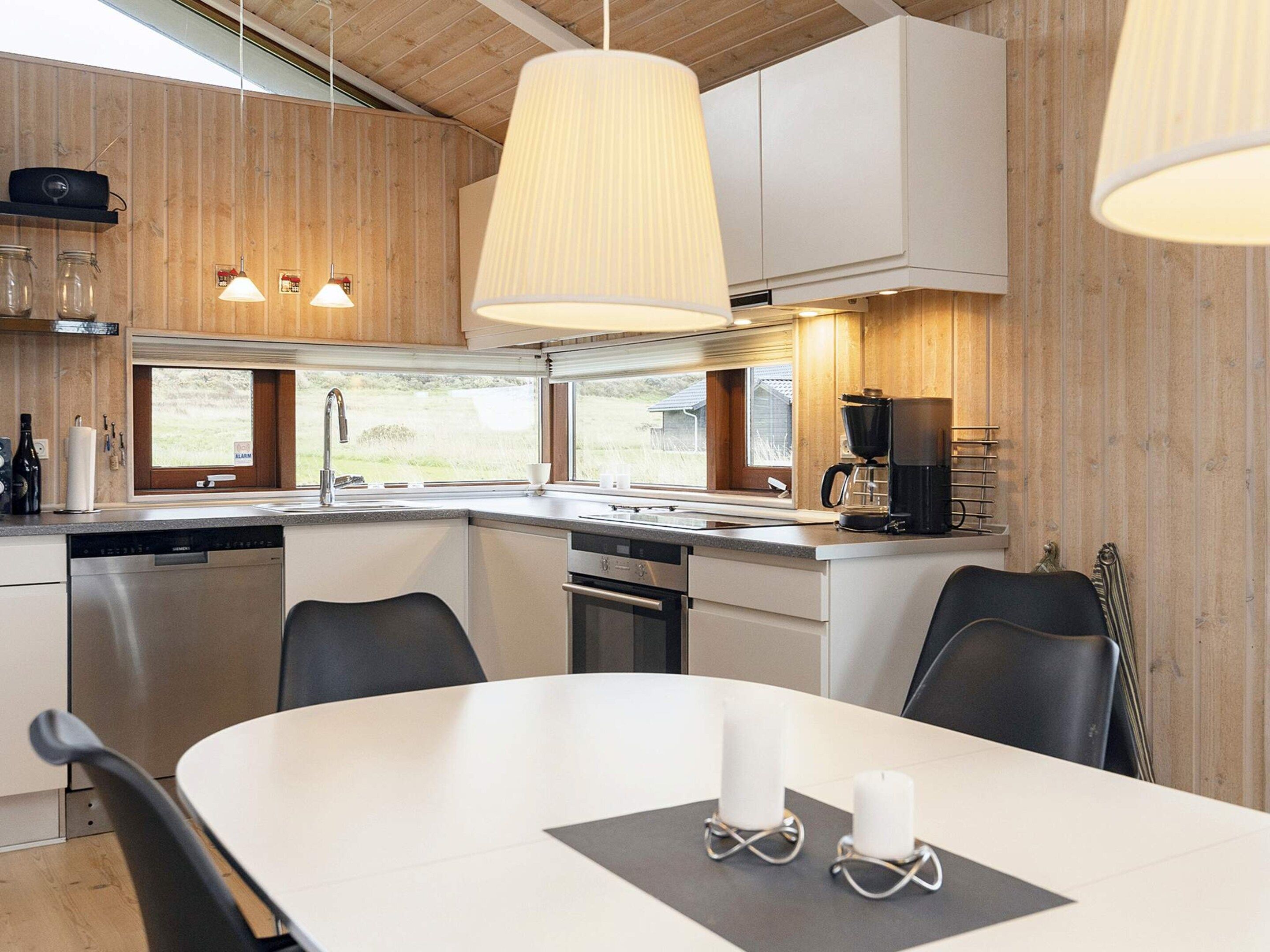 Cozinha moderna com ilha central, iluminação pendente e vista para o exterior.