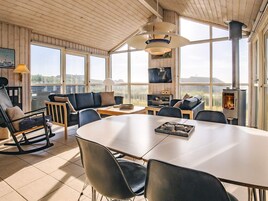 Um quarto espaçoso com uma grande mesa de jantar, assentos confortáveis, televisão e uma lareira a lenha.