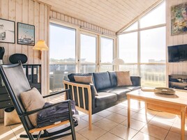 Um quarto com teto de madeira, sofá, cadeira, mesa e janelas amplas.
