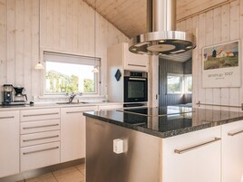Cozinha moderna com ilha central, forno embutido e iluminação pendente.