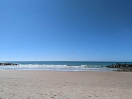 Uma praia com céu claro, mar calmo e costa rochosa.