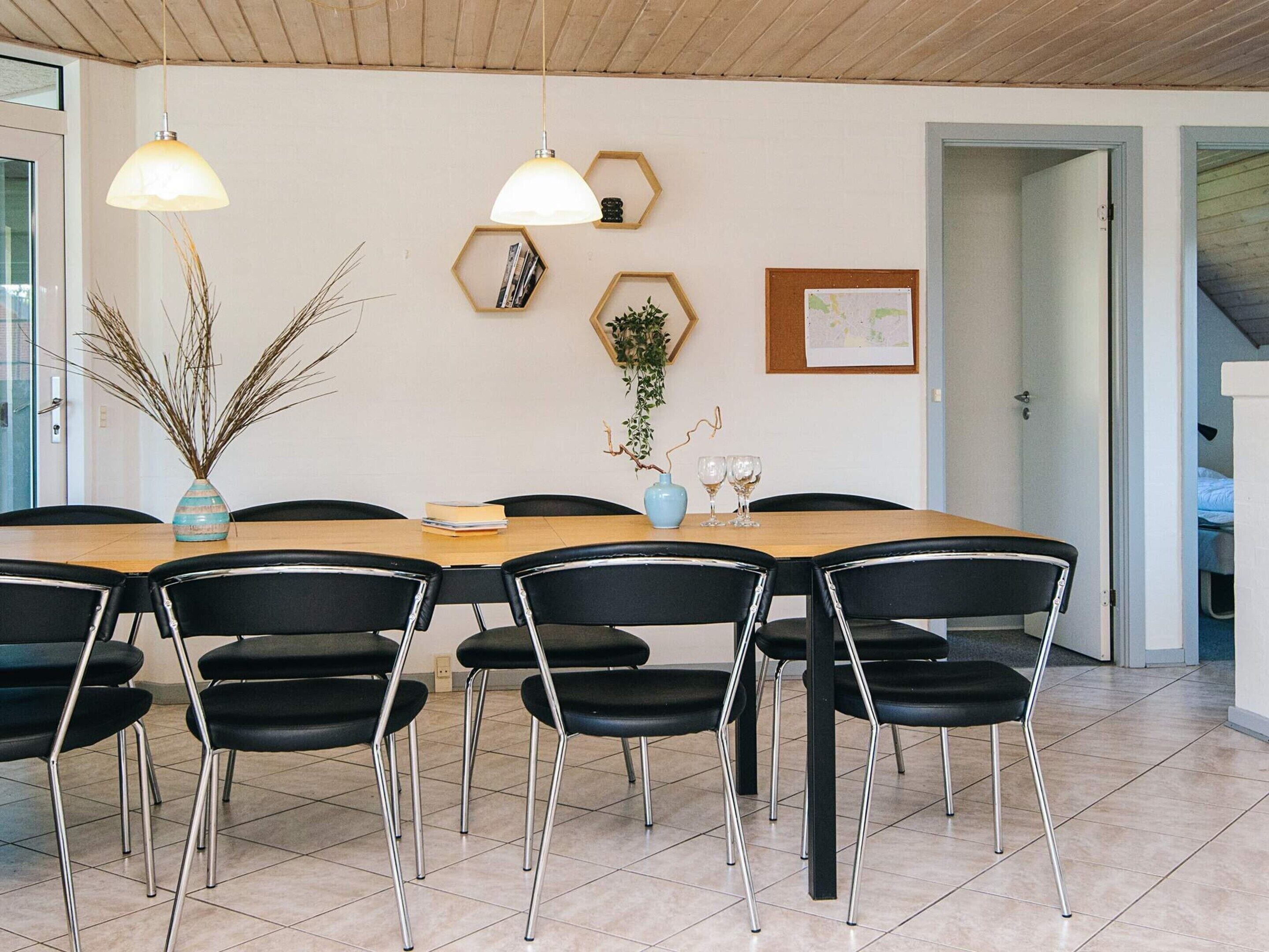 Uma sala de jantar com mesa de madeira, cadeiras pretas e luminárias pendentes.
