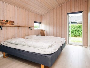 Quarto com cama de casal, paredes de madeira, janela e vista para o verde lá fora.