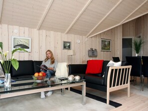 Uma sala de estar moderna com uma mesa de centro de vidro, sofás preto e branco e teto de madeira.