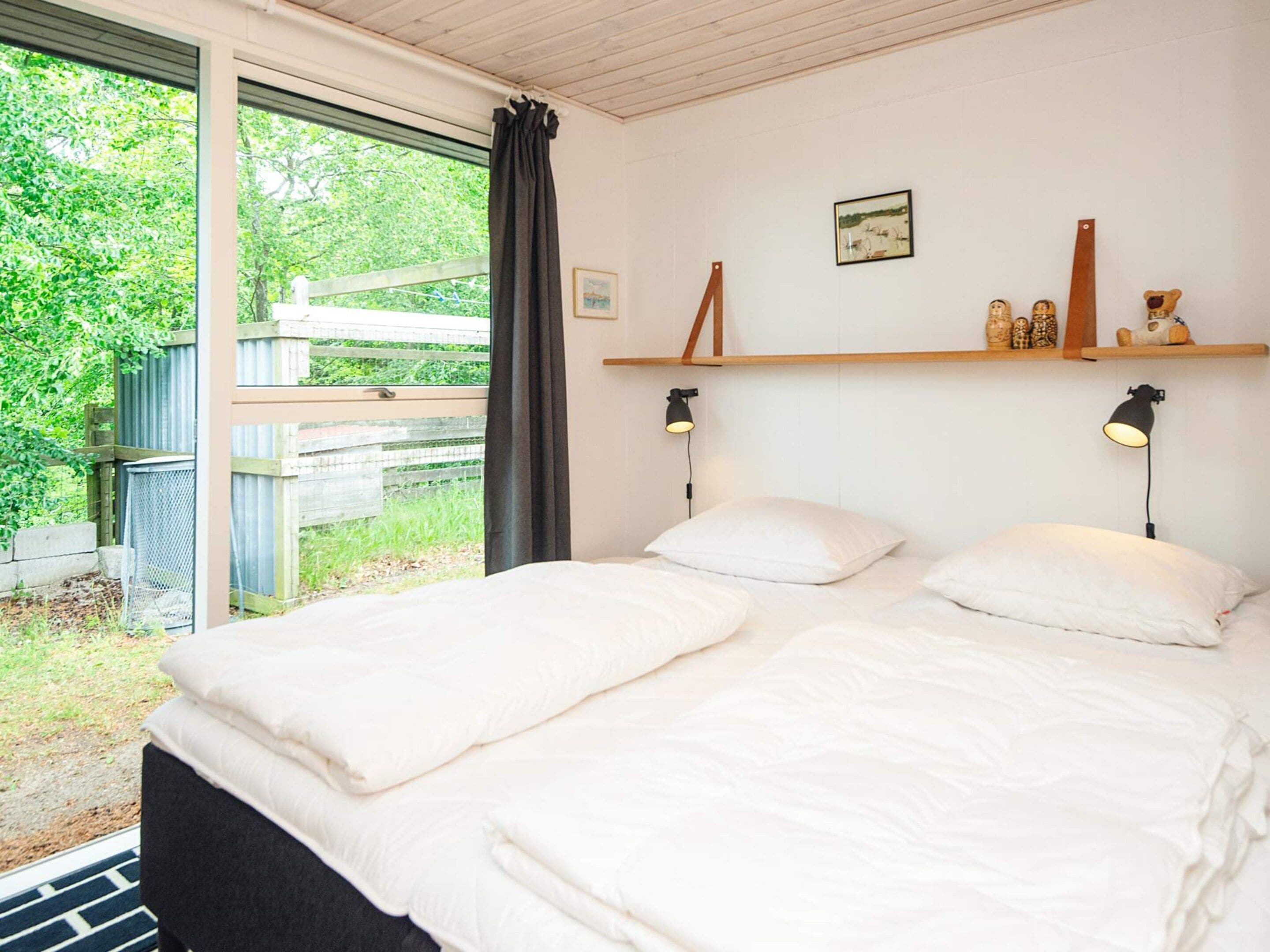 Quarto com cama, duas luminárias de cabeceira, janela com cortinas e prateleira com objetos decorativos.