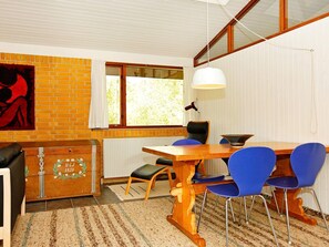 Uma área de jantar com uma mesa de madeira, cadeiras azuis, uma luminária pendente branca e um radiador.