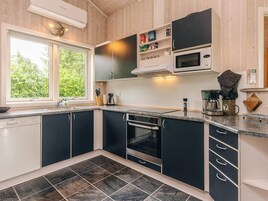 Cozinha moderna com armários escuros, forno embutido, micro-ondas e janela com vista para o verde lá fora.