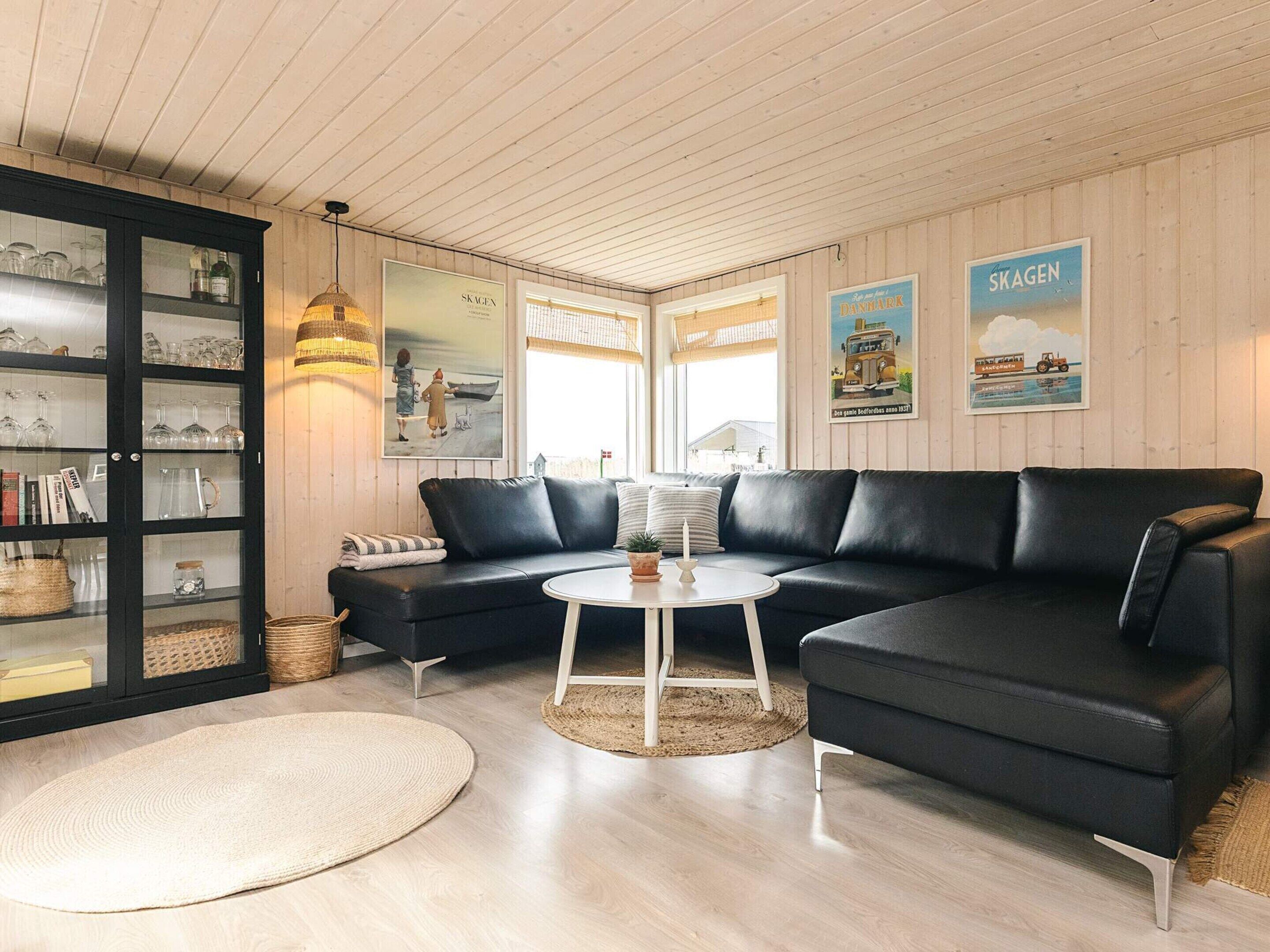Uma sala de estar moderna com um sofá de couro preto, um aparador de vidro com objetos decorativos e uma mesa de centro redonda.