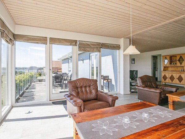 Uma sala de estar ampla, com um sofá de couro, uma mesa de centro de madeira e vista para o exterior.