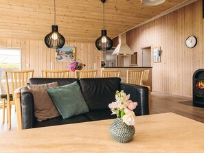 Uma sala de estar aconchegante, com um sofá de couro preto, mesa de jantar de madeira e um vaso com flores.