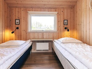 Quarto com duas camas, paredes de madeira, uma janela e duas luminárias fixadas na parede.