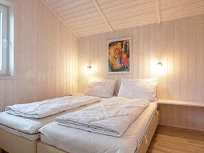 Quarto com duas camas, paredes de madeira, um quadro e duas luzes na parede.