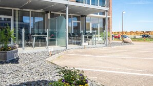 Um edifício moderno com fachada de vidro, área de estar ao ar livre e estacionamento.