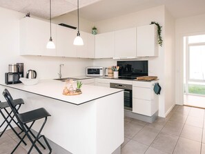 Uma cozinha moderna com armários brancos, uma ilha central, micro-ondas, cafeteira e pia.