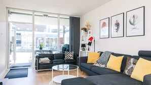 Sala moderna com sofá, mesa de centro e área de jantar visível por grandes portas deslizantes.