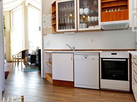 Cozinha compacta equipada com lava-louças, forno e armário com copos e pratos.