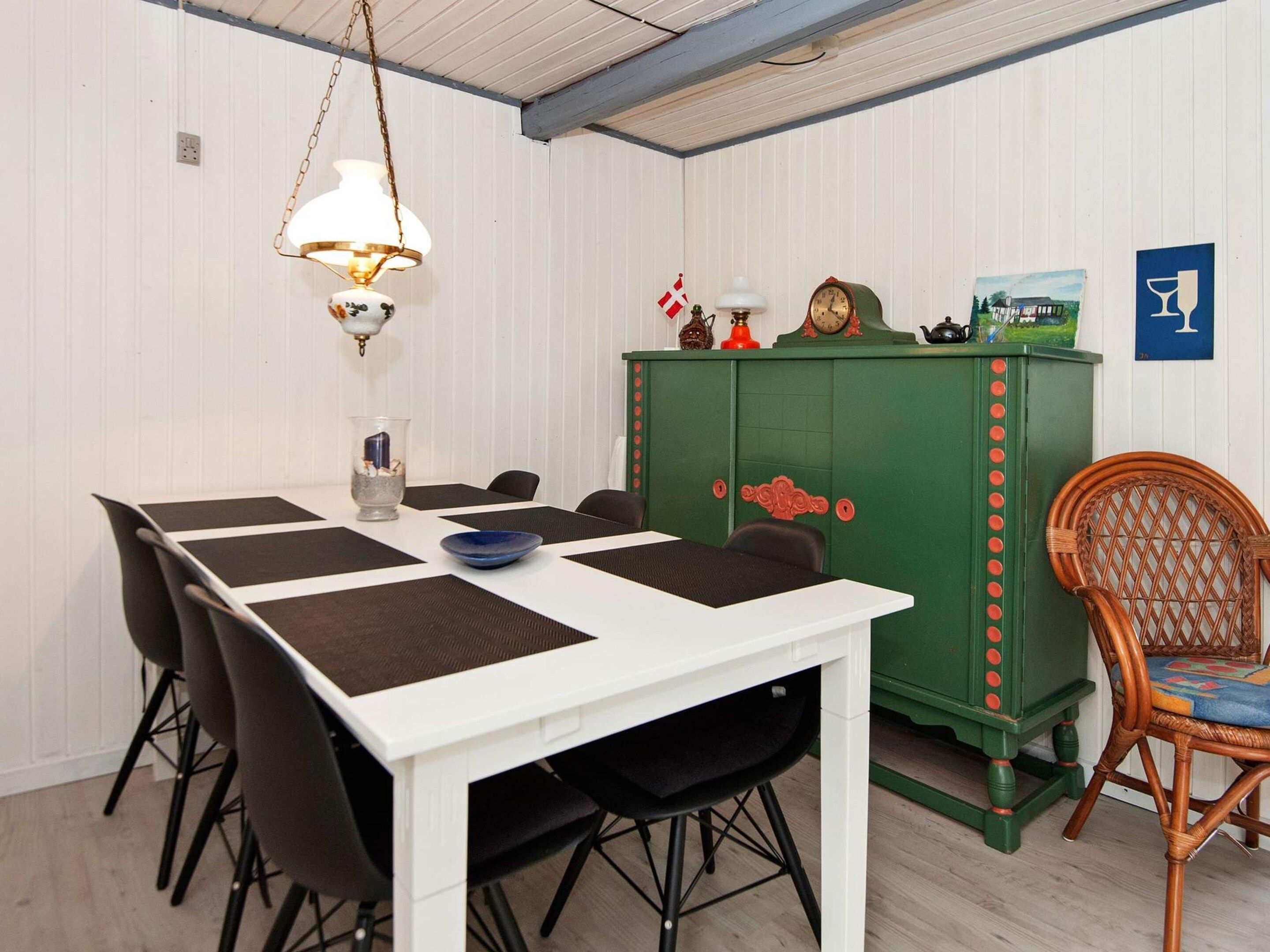 Uma área de refeições com uma mesa branca, cadeiras pretas e um armário verde com objetos decorativos.