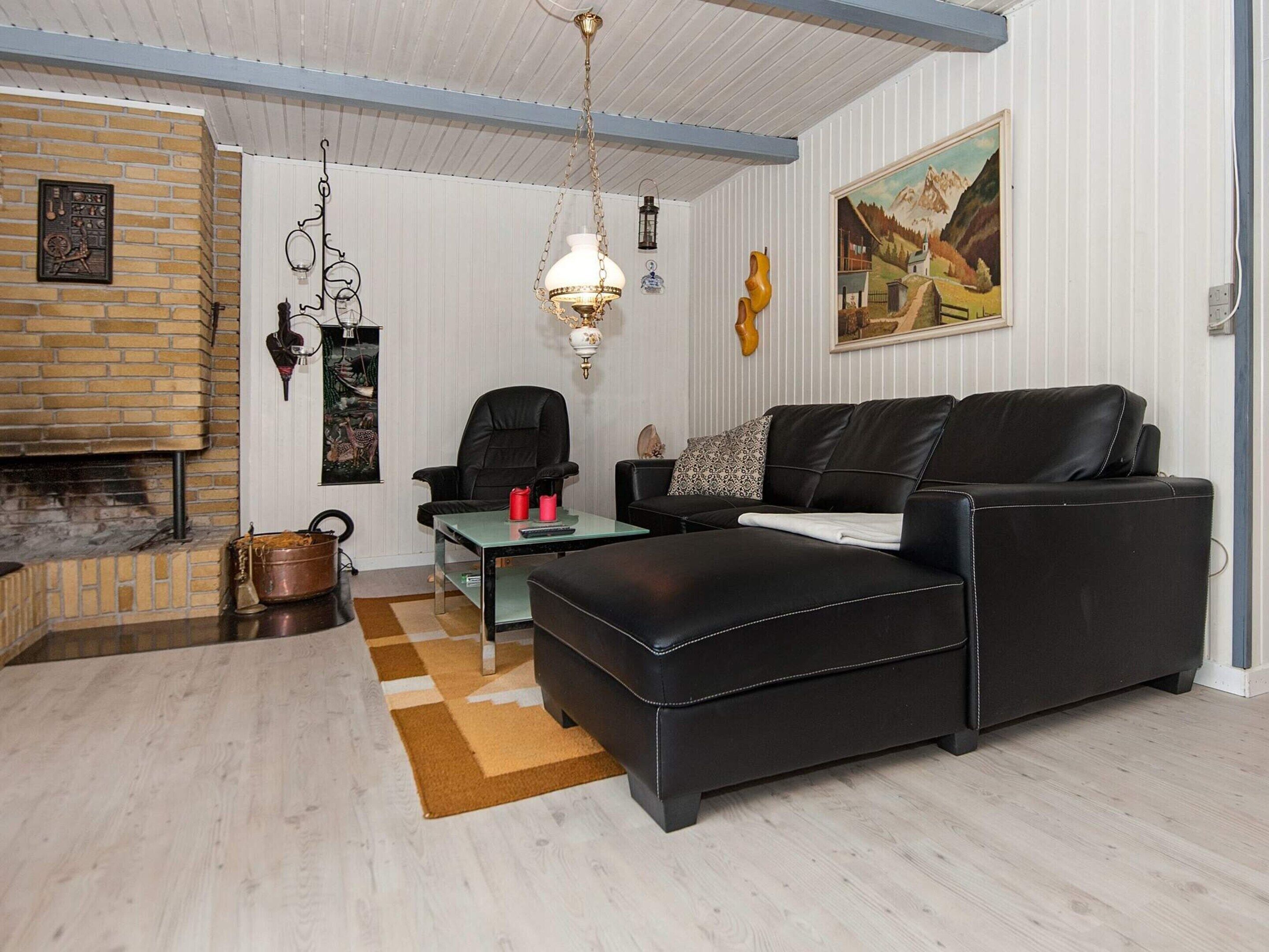 Uma sala de estar com lareira, um sofá de couro preto, uma mesa de centro de vidro e um quadro na parede.