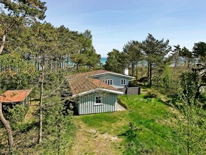 Uma casa de dois andares com telhado inclinado, cercada por árvores e um gramado.