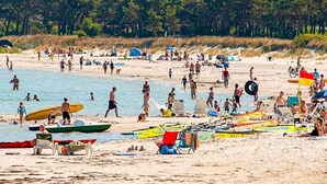 Uma praia cheia de gente, barcos e cadeiras de praia.