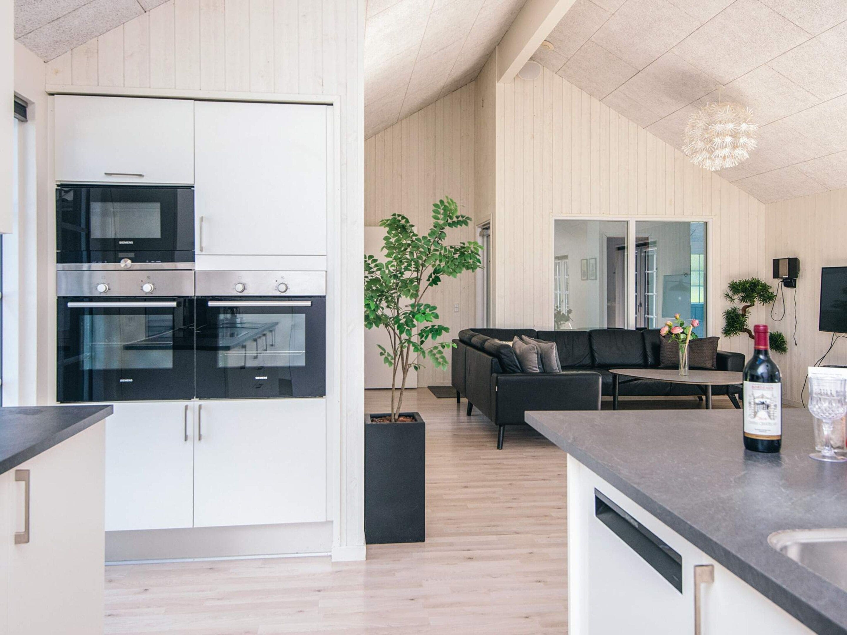 Cozinha moderna com eletrodomésticos embutidos, área de jantar com sofá e mesa, e sala de estar com televisão.