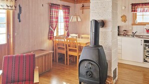 Um quarto acolhedor com uma mesa de jantar de madeira, cadeiras, uma poltrona listrada de vermelho e um fogão a lenha preto.
