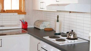 Cozinha com armários brancos, fogão e janela com cortina xadrez.