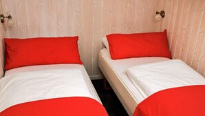 Duas camas de solteiro com roupa de cama vermelha em quarto com paredes de madeira e duas luminárias fixadas na parede.
