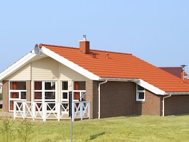 Uma casa de dois andares com telhado de telhas vermelhas, fachada de tijolos e varanda branca com corrimão.