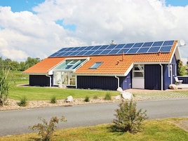 Uma casa com telhado inclinado, painéis solares, porta de vidro e um pequeno alpendre.