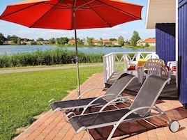 Um pátio com cadeiras de descanso e um guarda-sol, com vista para um lago e casas ao fundo.